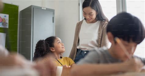 젊은 아시아 여성 교사가 교실에서 아프리카계 미국인 소녀를 가르치고 있다 국제 학교의 다양한 다민족 학생들 사진