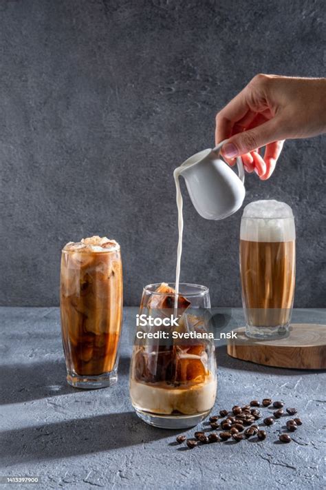 어두운 테이블에 아이스 커피에 우유를 붓고 있습니다 크림을 붓고 커피 원두를 얹은 키 큰 유리에 아이스 커피 복사 공간이있는 어두운 배경에서 차가운 코피 음료를 마신다
