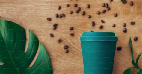 볶은 커피 원두와 녹색 몬스테라 잎이 있는 나무 배경에 세련된 재사용 가능한 에코 커피 컵 일회용 플라스틱 금지 폐기물 제로 개념 플랫 레이 지속 가능한 라이프