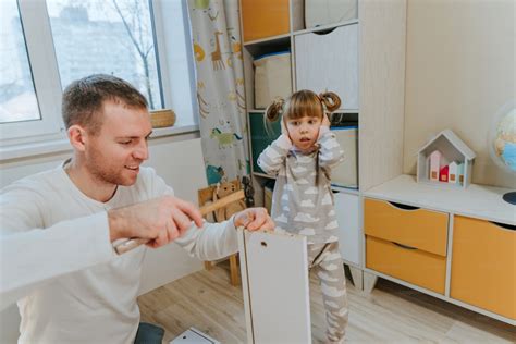 어린 4 살 소녀는 시끄러운 소음 때문에 손으로 귀를 닫았고 아버지는 아이 침실에서 침대 서랍을 고정하기 위해 망치를 사용합니다