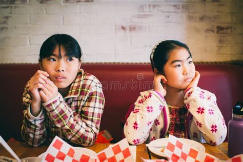 Two Asian Girls Dressed In Winter Clothe Sitting At A Table In A