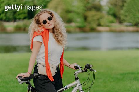 Pretty Woman Rides Bicycle Has Bushy Blonde Hair Stands Near Her Bike