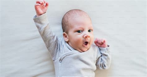 줄무늬 옷을 입은 귀여운 신생아가 침대에 누워 팔을 올리고 슈퍼히어로 포즈를 취하고 입을 벌리고 있다 사진 Unsplash의 초상 이미지