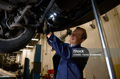 수리소에서 자동차 유지 보수 및 보증 수리 기술자는 작업장 차고에서 리프트에서 들어 올린 자동차의 휠 정렬을 위해 섀시를 확인하는 손전등 램프를 사용합니다 자동 서비스