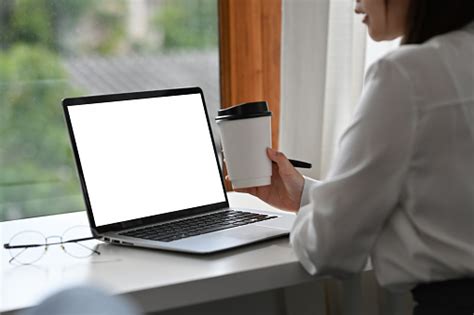 현대식 창가 책상에서 노트북과 테이크아웃 커피잔을 들고 원격으로 일하는 사업가의 클로즈업 이미지 모형 또는 디자인을 위한 빈 화면 노트북 계획에 대한 스톡 사진 및 기타