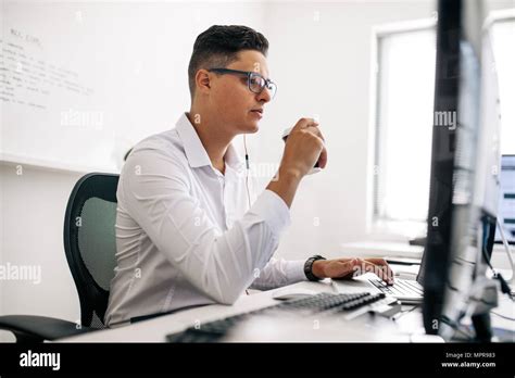 smiling software developer sitting at his office desk working on laptop