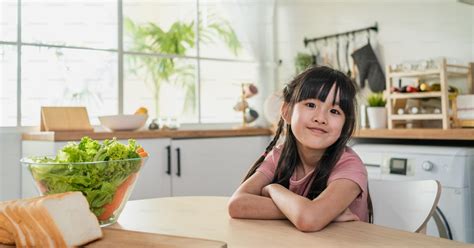 아시아의 어린 아이의 초상화는 미소를 지으며 부엌에서 카메라를 본다 사랑스러운 여자 아이들은 테이블에 앉아 행복을 느끼고 집에서 아침 주말을 즐깁니다 집에서 여가 활동