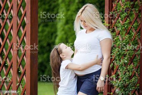 아름 다운 임신한 여자와 작은 딸입니다 귀여운 어린 소녀는 여름 자연에 그녀의 임신 어머니를 포옹 가정 생활에 대한 스톡 사진