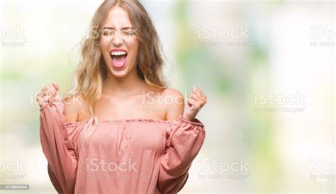 무기와 성공에 대 한 흥분된 격리 된 배경 위에 아름 다운 젊은 금발의 여 자가 축 하 승리 미소 발생합니다 우승자 개념입니다 곱슬 머리에 대한 스톡 사진 및 기타 이미지