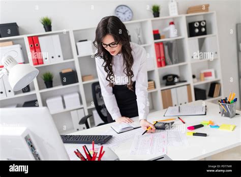 A Beautiful Young Girl Stands Bent Over An Office Desk Holds A Pen In