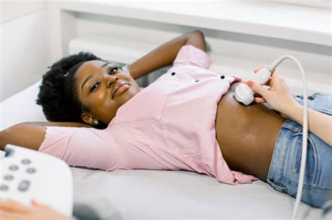 병원에서 젊은 아프리카 여성 환자의 복부를 검사하는 동안 손에 초음파 스캐너를 들고 직장에서 초음파 기계를 사용하여 의사 초음파