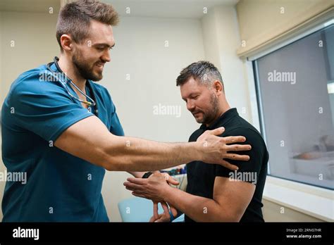 Man Sitting On Examination Couch While Physical Therapist Assessing His