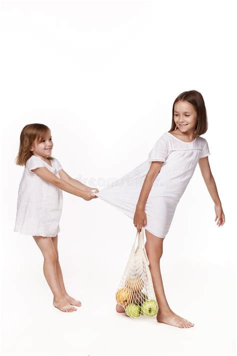 Dos Hermanas La Hermana Mayor Sostiene Una Bolsa De Fruta Y La Menor La Empuja Por El Vestido