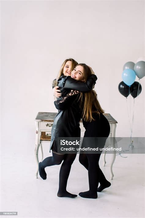 검은 드레스를 입은 두 명의 젊은 예쁜 여성이 함께 풍선을 들고 흰색에 고립 된 옷장이있는 빈티지 흰색 테이블 근처에서 암탉이나
