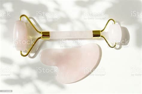 핑크 구아 샤 마사지 도구입니다 로즈 쿼츠 롤러 흰색 배경에 나뭇잎의 회색 그림자입니다 가정에서의 페이셜 스킨 케어 안티 에이징 및 리프팅 요법 이미지 그늘에 대한 스톡