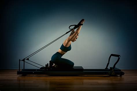 개혁가 침대와 필라테스 운동을하고 어린 소녀 개혁가 회색 배경 낮은 키 예술 조명에 아름 다운 슬림 피트 니스 트레이너 피트니스 컨셉 필라테스에 대한 스톡 사진 및 기타