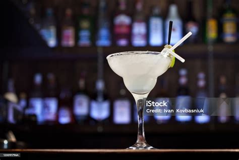 바 카운터에서 화이트 칵테일 마티니 진 데킬라 라임과 함께 술을 마시는 병을 배경으로 마십니다 나무 판에 술이 있는 유리 자외선 조명이 있는 파란색 배경입니다 0명에 대한