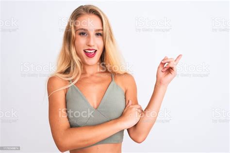 고립된 흰색 배경 위에 서있는 캐주얼 한 녹색 티셔츠를 입은 젊은 아름다운 여성은 얼굴에 큰 미소를 지으며 카메라를 바라보는