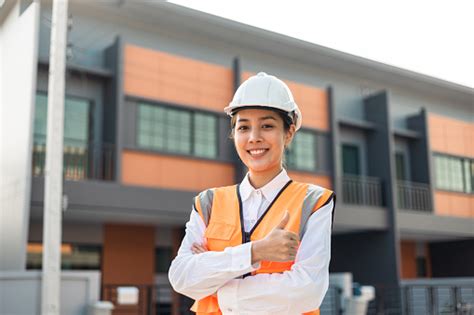 현대 주택 건설 현장에 서 있는 자신감 있는 엔지니어 여성 건설 현장에서 흰색 안전 헬멧을 쓴 건축가 정비공 서비스 공장 제복을 입은 전문 작업 직업 개발에 대한 스톡 사진