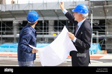Two Architect Developers Reviewing Building Plans At Construction Site