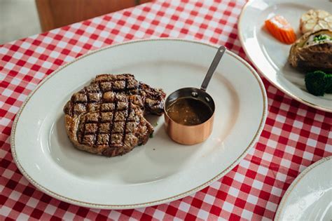 숯불 구이 Wagyu Ribeye 스테이크 바베 큐 소스와 함께 제공 하 고 빨간색과 흰색 패턴 식탁보에 흰색 접시에 감자를 구운 갈비 음식에 대한 스톡 사진 및 기타