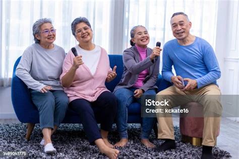 행복한 아시아 선배 친구들이 행복한 웃는 얼굴로 거실 소파에서 노래방을 부르고 있다 노래방에서 노래하는 노인들 집에서 노래방에서 노래하는 친구들 55 59세에 대한 스톡