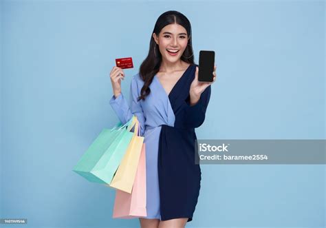 파란색 배경에 고립 된 쇼핑백을 들고 신용 카드와 스마트 폰을 보여주는 행복한 아름다운 아시아 여성 25 29세에 대한 스톡 사진 및 기타 이미지 Istock