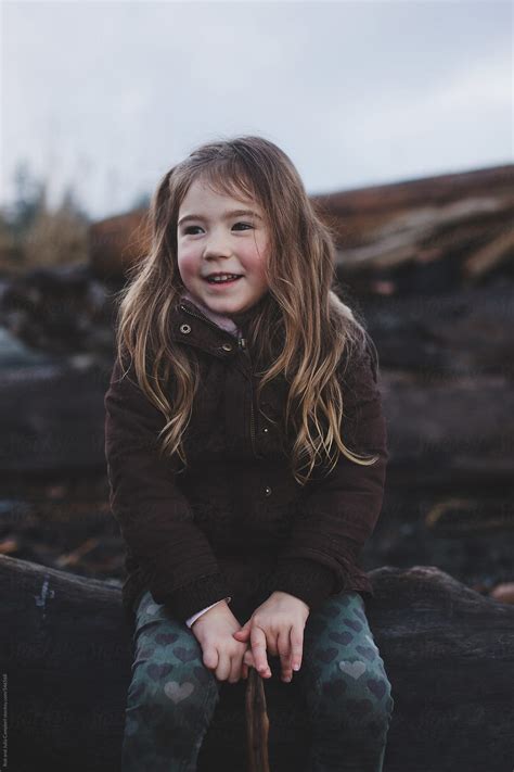 Cute Young Girl Sitting On Logs In West Coast Winter By Stocksy