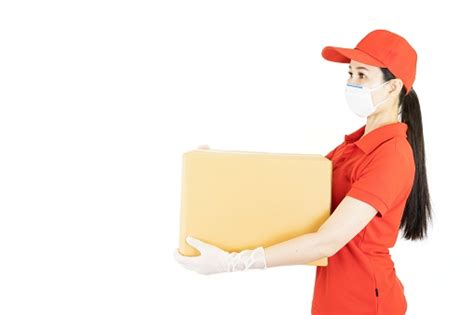 흰색 배경에 고립 된 마스크를 입고 빨간 유니폼을 입은 배달 여성 모자 티셔츠 청바지 택배 또는 골판지 상자를 들고 딜러로 일하는 여성 패키지를 수신합니다 광고 용 공간