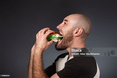 패스트 푸드와 생태의 개념 수염을 가진 대머리 남자는 행복하게 쓰레기로 채워진 햄버거를 먹고 그로테스크하게 확대된 턱 검은 색 배경 복사 공간 먹기에 대한 스톡 사진 및