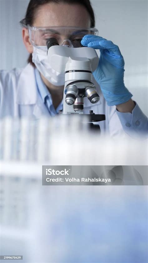 파란 장갑 보호 안경 의료용 마스크를 착용한 여성 과학자가 현대 실험실 환경에서 현미경을 사용하고 있습니다 낮은 키 조명 사진 과학 및 의학 Stem 주제에 대한 스톡 사진