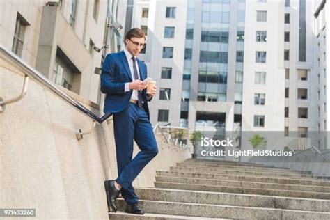 종이 컵 커피 비즈니스 빌딩 근처 계단에 스마트폰을 사용 하 여 세련 된 정장에 매력적인 젊은 사업가 수트에 대한 스톡 사진 및 기타 이미지 Istock