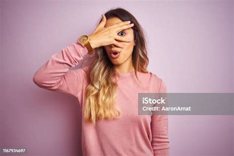 분홍색 고립 된 배경 위에 스웨터를 입은 젊은 아름다운 여성은 얼굴과 눈을 손으로 덮고 부끄러운 표정으로 손가락을 통해 들여다 봅니다 가리기에 대한 스톡 사진 및 기타