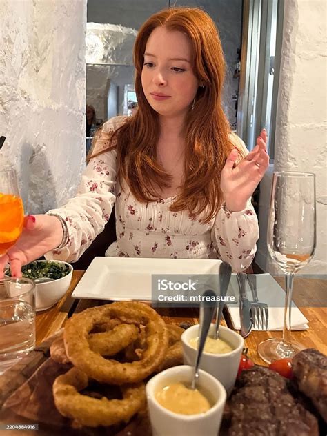 클로즈업 이미지 매력적인 빨간 머리의 여성 스프릿츠 베네치아노 칵테일 음료 종이 빨대 얼음 조각 오렌지 조각 발렌타인 데이 데이트 반죽 양파 링 방울 토마토 디핑 소스를