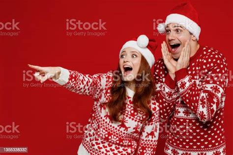 젊은 부부 친구 두 남자 여자 에 스웨터 모자 포인트 검지 손가락 옆으로 지역 보유 얼굴 격리 에 일반 빨간 배경 스튜디오 새해 복 많은 2022 축하 메리 호 X마스 휴가