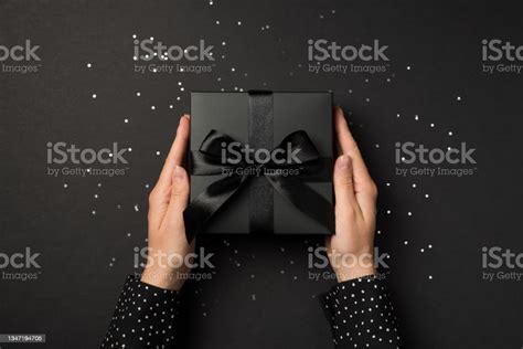 고립된 검은 색 배경에 반짝이는 스팽글 위에 검은 색 선물 상자를 들고 있는 물방울 무늬 셔츠를 입은 1인칭 탑 뷰 사진 개인적 시점에 대한 스톡 사진 및 기타 이미지