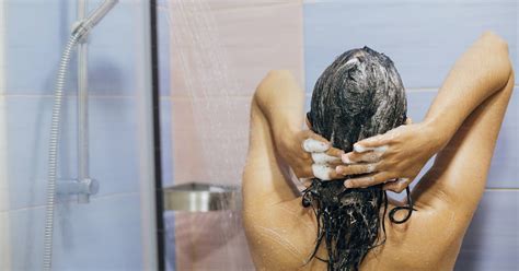 젊은 행복한 여자는 샴푸로 머리를 씻고 거품으로 젖은 머리를 감쌉니다 샤워를 하고 시간을 즐기는 아름다운 갈색 머리 소녀의 뒤 몸과 모발 위생 라이프스타일 개념