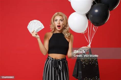 빨간 벽 배경에 고립 된 포즈 검은 옷을 입고 충격 젊은 여자 소녀 쇼핑 할인 판매 개념 복사 공간을 모의합니다 현금 돈의 구매 팬과 함께 공기 풍선 패키지 가방을 들고