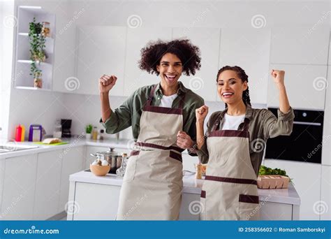 Photo Of Confident Lucky Wife Husband Dressed Aprons Rising Fists Cooking Lunch Indoors Home