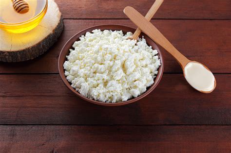 코 티 지 치즈와 크림입니다 부드러운 치즈와 꿀 나무 보드에 도자기에 코 티 지 치즈입니다 나무로 되는 숟가락에 크림입니다 나무 스탠드에 여 보 공간 복사 갈색에 대한 스톡