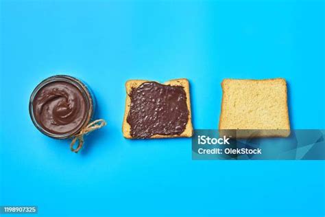 바닐라 빵 조각 근처에 녹은 초콜릿이 가득한 유리 항아리가 부엌의 파란색 책상 위에 놓여 있습니다 영양가있는 아침 식사 또는 점심 의 개념 맨 위 보기 가득 찬에 대한 스톡