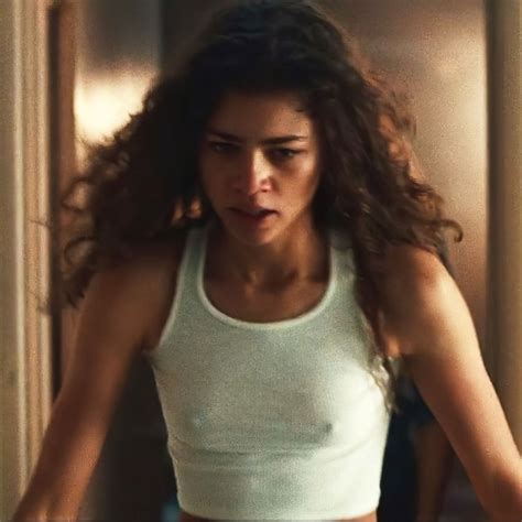 A Woman With Long Brown Hair Wearing A White Tank Top And Black Shorts In A Hallway