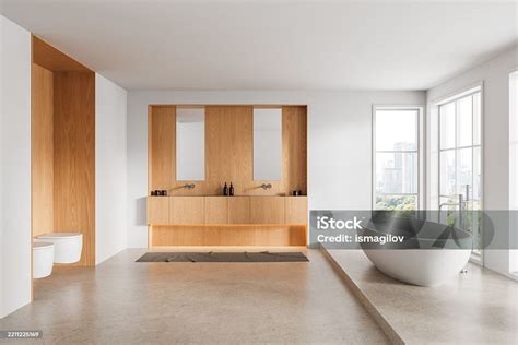 현대적인 미니멀리스트 욕실 인테리어에는 목재 세면대 흰색 독립형 욕조 대낮에 도시 경관이 내려다보이는 대형 창문이 있습니다 3d