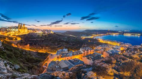 Skyline View Of Mellieħa Town After Sunset With Parish Church And Beach