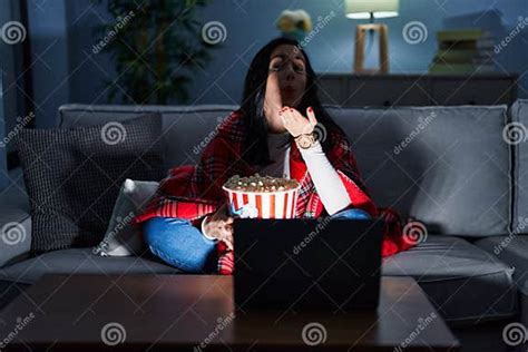 Hispanic Woman Eating Popcorn Watching A Movie On The Sofa Looking At