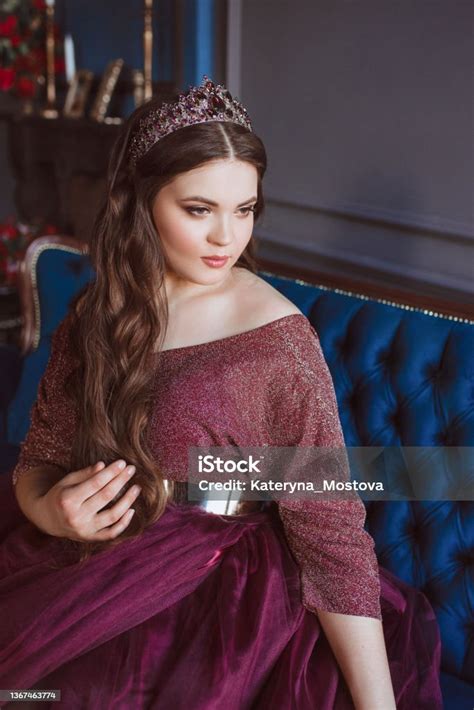 긴 보라색 여왕의 드레스와 크라운에 아름다운 젊은 예쁜 귀여운 여자 공주 의 초상화 긴 머리와 파란색 벨벳 소파에 앉아 메이크업 20 24세에 대한 스톡 사진 및 기타