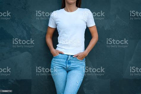 빈 흰색 티셔츠와 청바지를 입은 젊은 여성이 회색 벽에 포즈를 취하고 있다 디자인 프린트 또는 티셔츠 프린트 스토어용 모형 T 셔츠에 대한 스톡 사진 및 기타 이미지