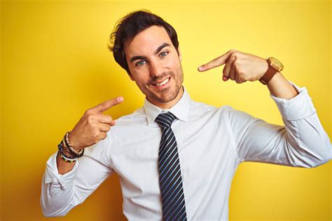 우아한 셔츠를 입고 고립 된 노란색 배경에 넥타이를 매고 손가락 이빨과 입으로 가리키는 쾌활한 미소를 짓고있는 젊은 잘생긴 사업가 치과 건강 개념 가리키기에 대한 스톡 사진