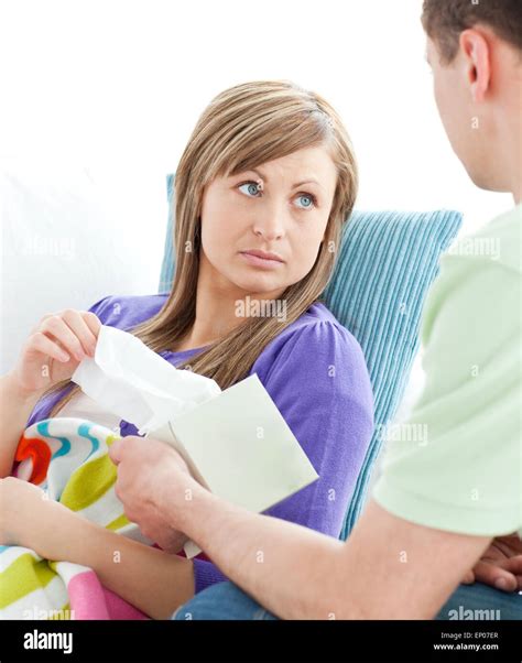 Assertive Man Giving His Ill Girlfriend Tissue Lying On A Sofa Stock
