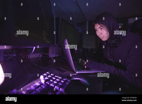 Asian Cyber Security Hacker Wearing Hood While Working On Programming In Dark Room Copy Space
